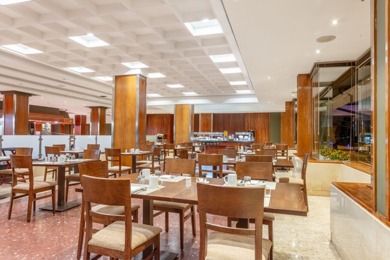 Um restaurante espaçoso com mesas e cadeiras de madeira, um balcão central e um design moderno no teto.