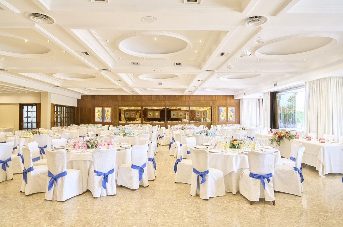 Uma sala de banquetes com mesas redondas, toalhas brancas e fitas azuis.