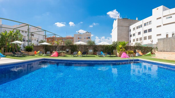 Piscina com espreguiçadeiras e guarda-sóis, cercada por edifícios e vegetação.