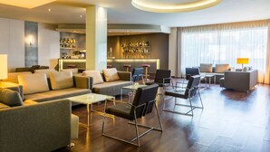 Um hall de hotel moderno com área de bar, opções de assento e uma grande luminária circular.