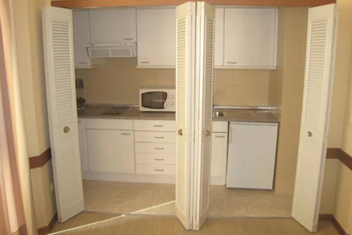 Cozinha compacta com armários brancos, micro-ondas e geladeira pequena.