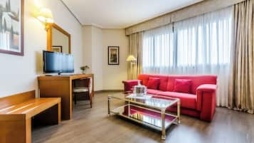 Quarto de hotel com televisão de tela plana, sofá vermelho, mesa de centro de vidro e escrivaninha de madeira.