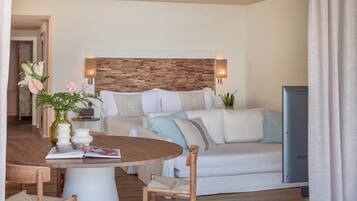 Quarto de hotel moderno com cabeceira de madeira, sofá branco, mesa de jantar com cadeiras e televisão de tela plana.