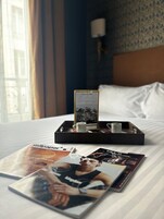 Cama bem arrumada com um tabuleiro de itens de café da manhã, incluindo uma xícara de café e um muffin, e duas revistas sobre a cama.