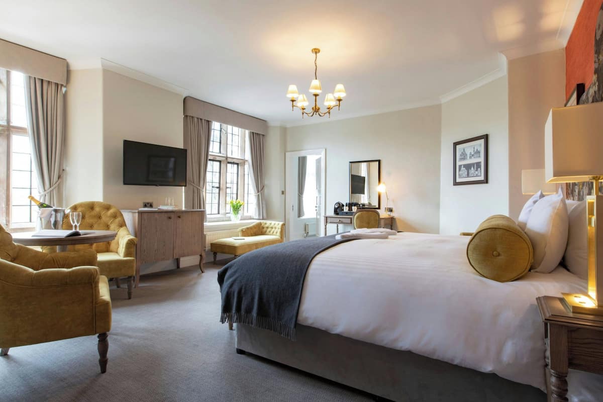 Quarto de hotel com uma cama grande, uma escrivaninha, uma cadeira, uma televisão e um candelabro.