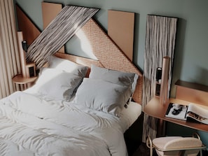 Quarto moderno com cama, almofadas, mesa de cabeceira, cadeira e arte abstrata na parede.