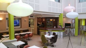 Um espaço interior moderno com área de bar, assentos com mesas e cadeiras, e luminárias decorativas pendentes.