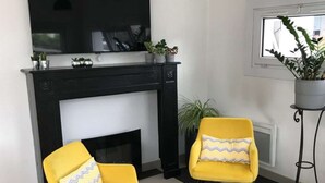 Uma sala de estar moderna com uma lareira preta, dois poltronas amarelas, uma luminária pendente preta e um vaso de planta perto da janela.