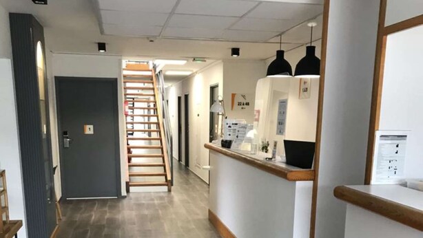 Corredor moderno de hotel com escada de madeira, balcão de recepção e área de bar.