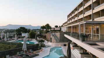 Um hotel moderno com piscina no terraço, área de estar ao ar livre e vista para as montanhas.