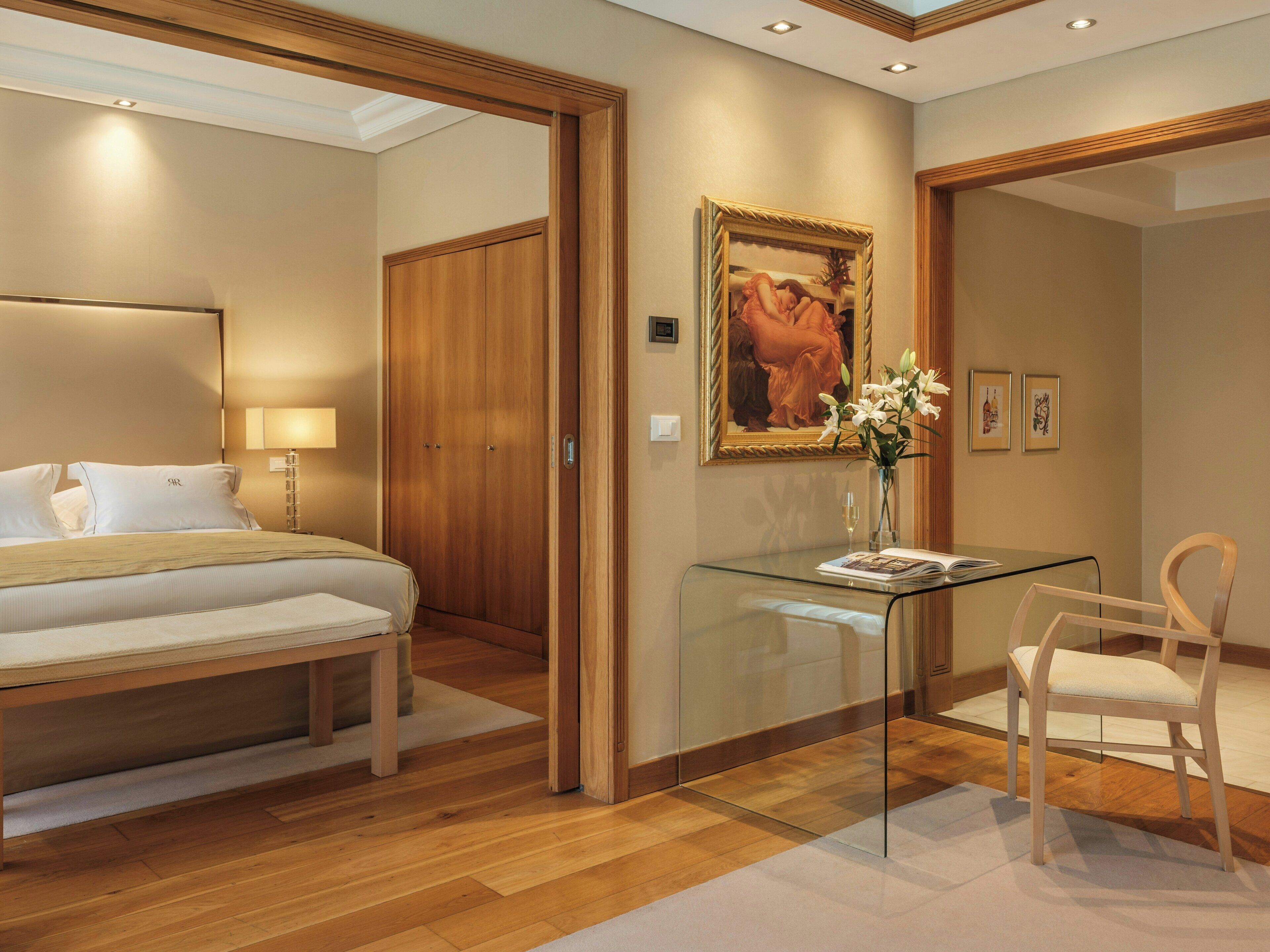 Quarto de hotel com cama, mesa de cabeceira, abajur, obra de arte emoldurada e uma cadeira.