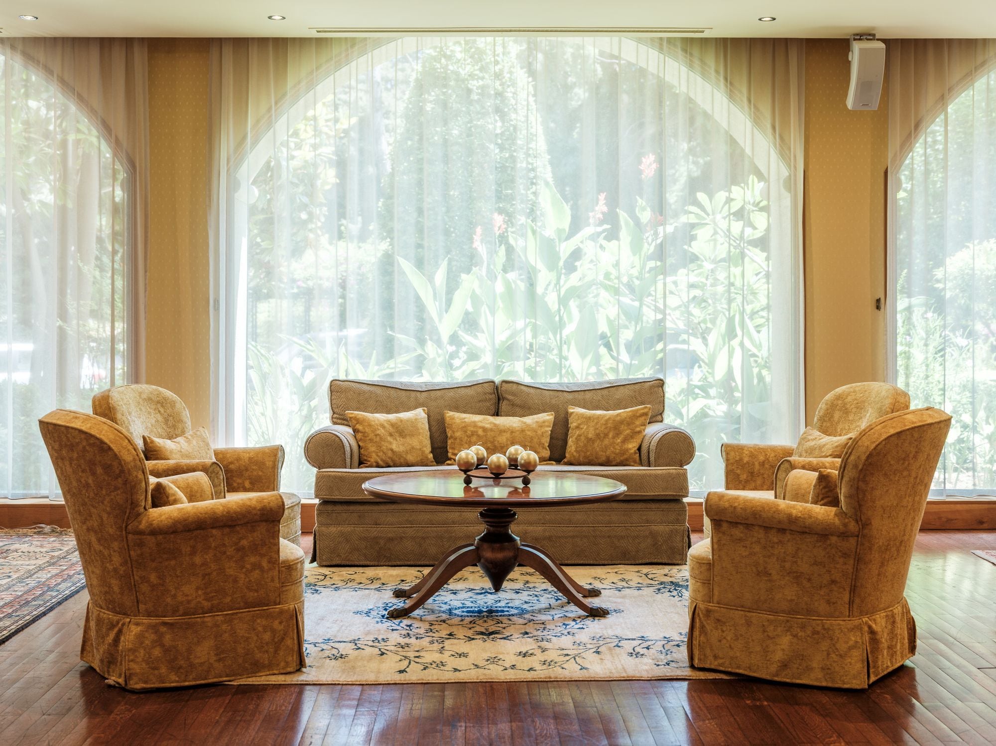Quarto com sofá, duas poltronas, mesa de centro e uma grande janela com cortinas.