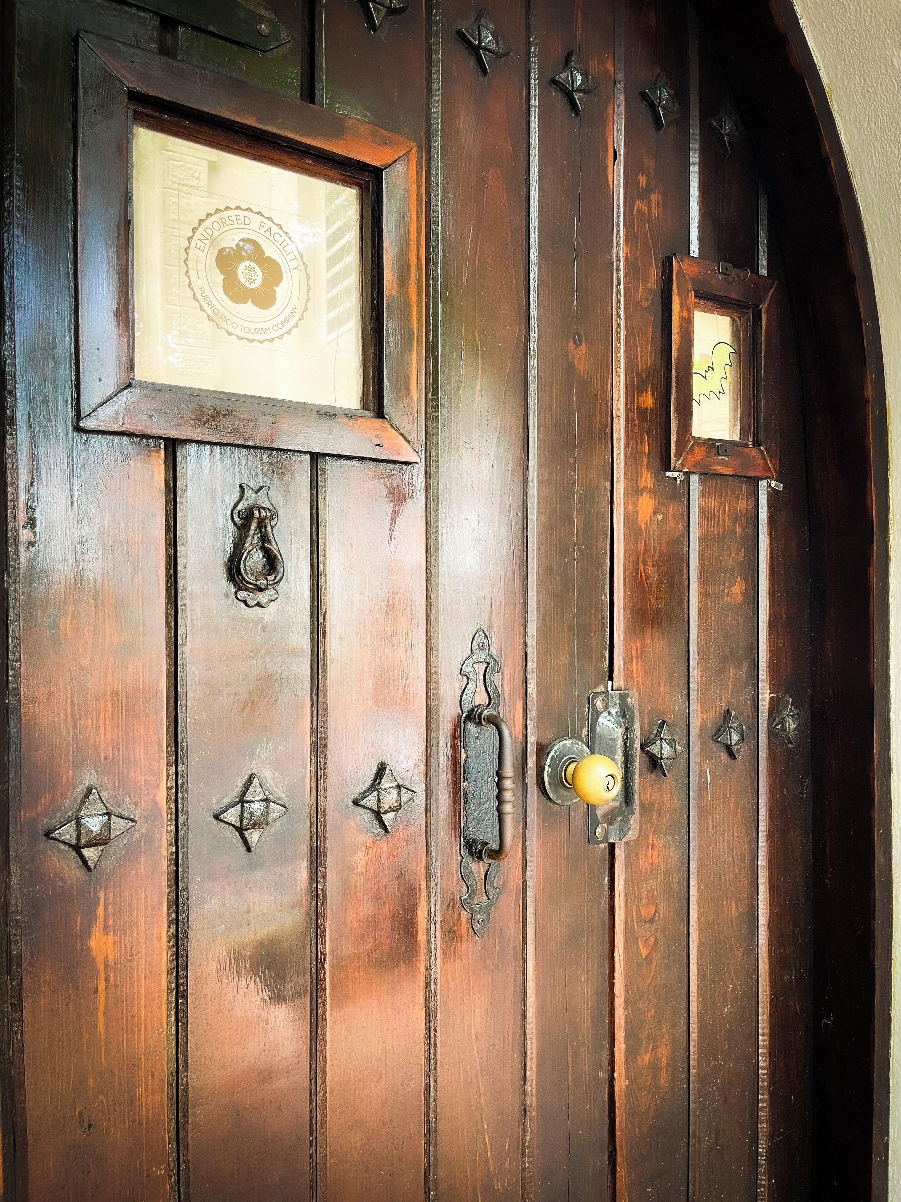 Uma porta de madeira com design antigo, exibindo uma placa emoldurada, puxadores metálicos decorativos e uma pequena janela.