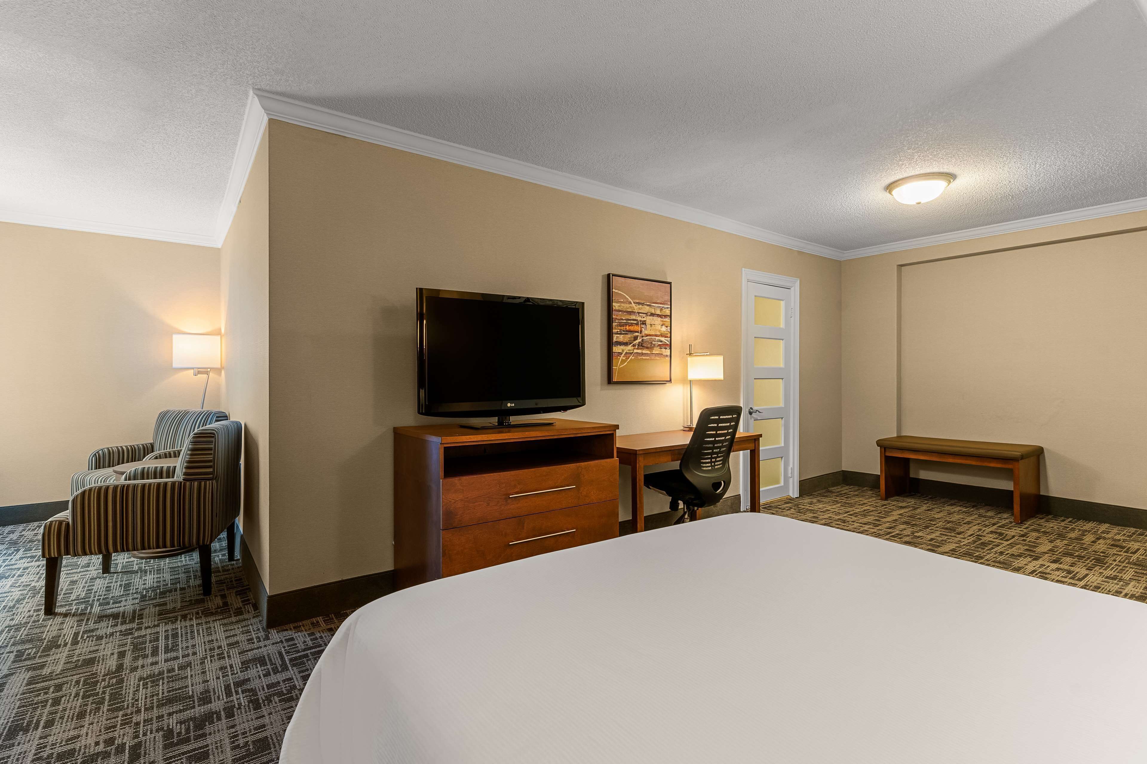 Quarto de hotel com cama, escrivaninha, televisão, cadeira e um banco.