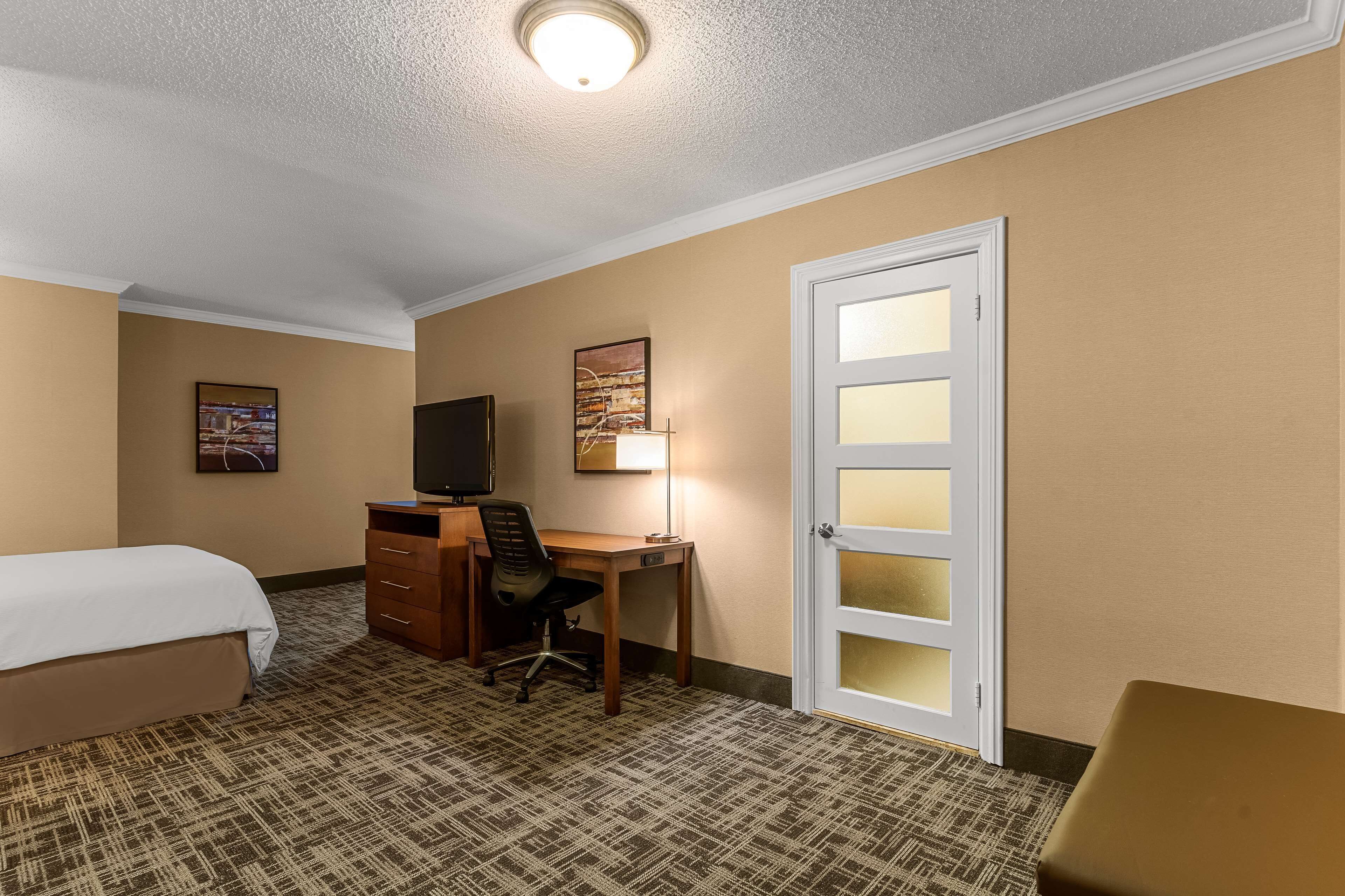 Quarto de hotel com uma cama, uma escrivaninha com cadeira, uma televisão e uma porta.