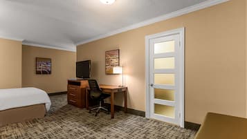 Quarto de hotel com uma cama, uma escrivaninha com cadeira, uma televisão e uma porta.