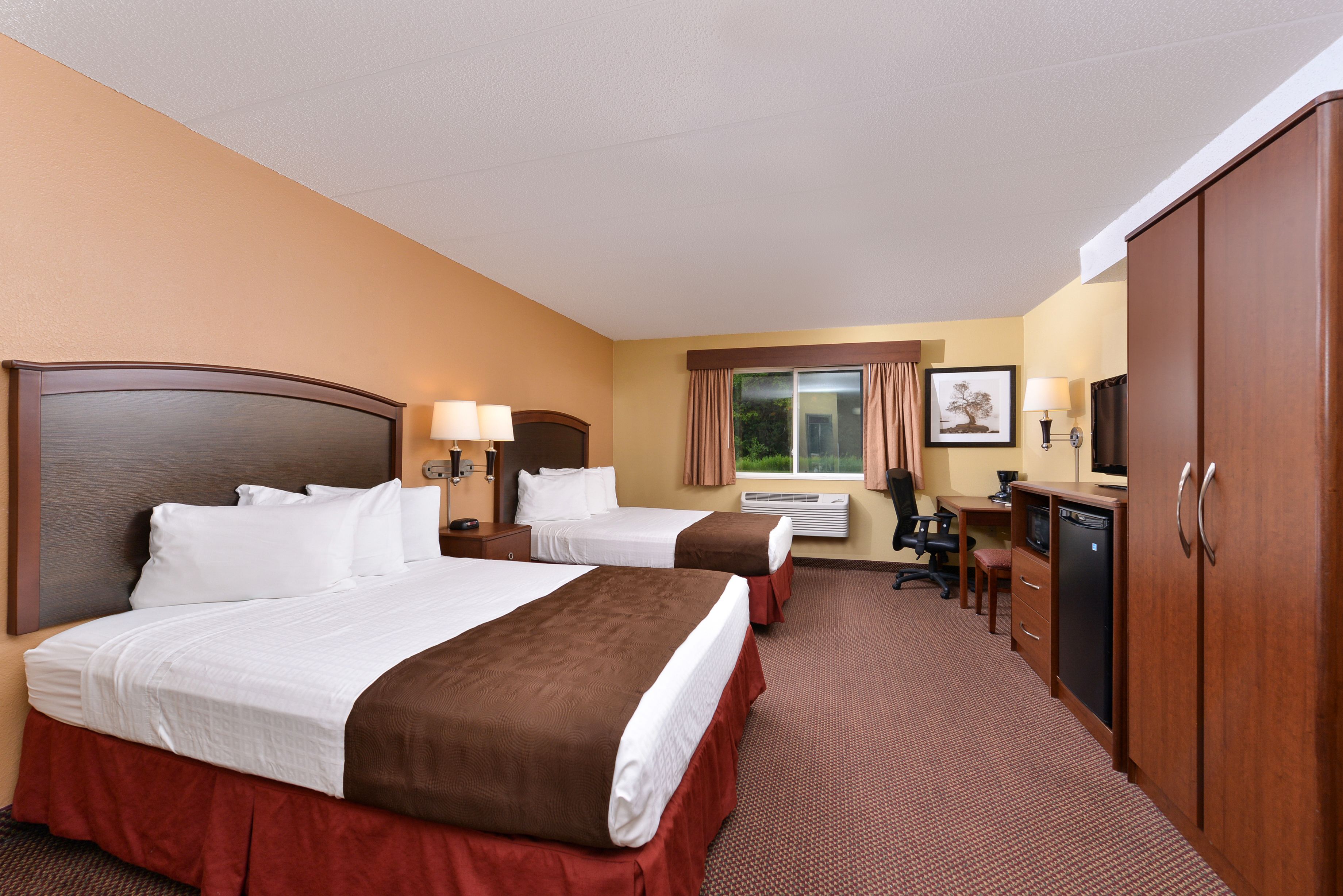 Quarto de hotel com duas camas, uma escrivaninha, uma cadeira, um guarda-roupa e uma televisão.