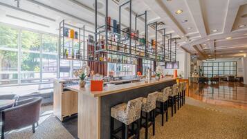 Uma área de bar moderna com balcão de madeira, vários bancos altos e uma variedade de garrafas e copos nas prateleiras.