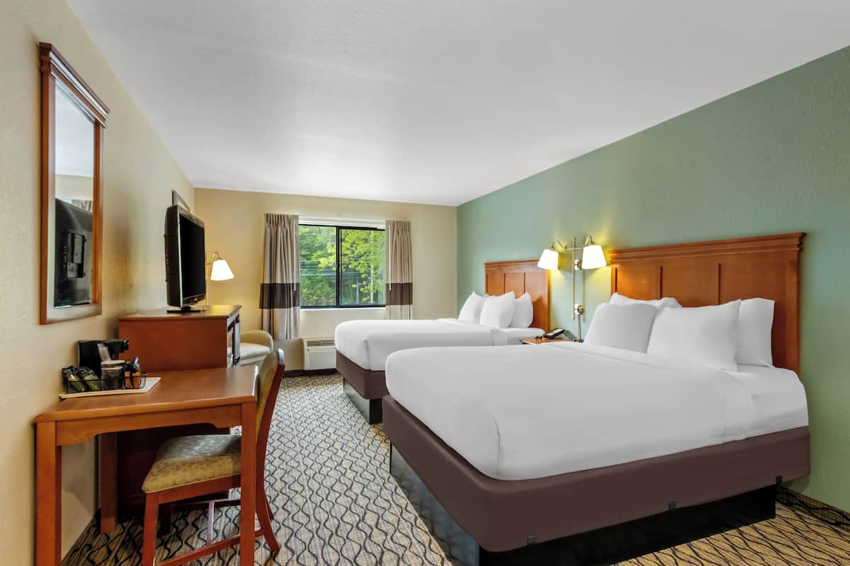 Quarto de hotel com duas camas, uma escrivaninha, uma cadeira, uma televisão e uma janela com cortinas.