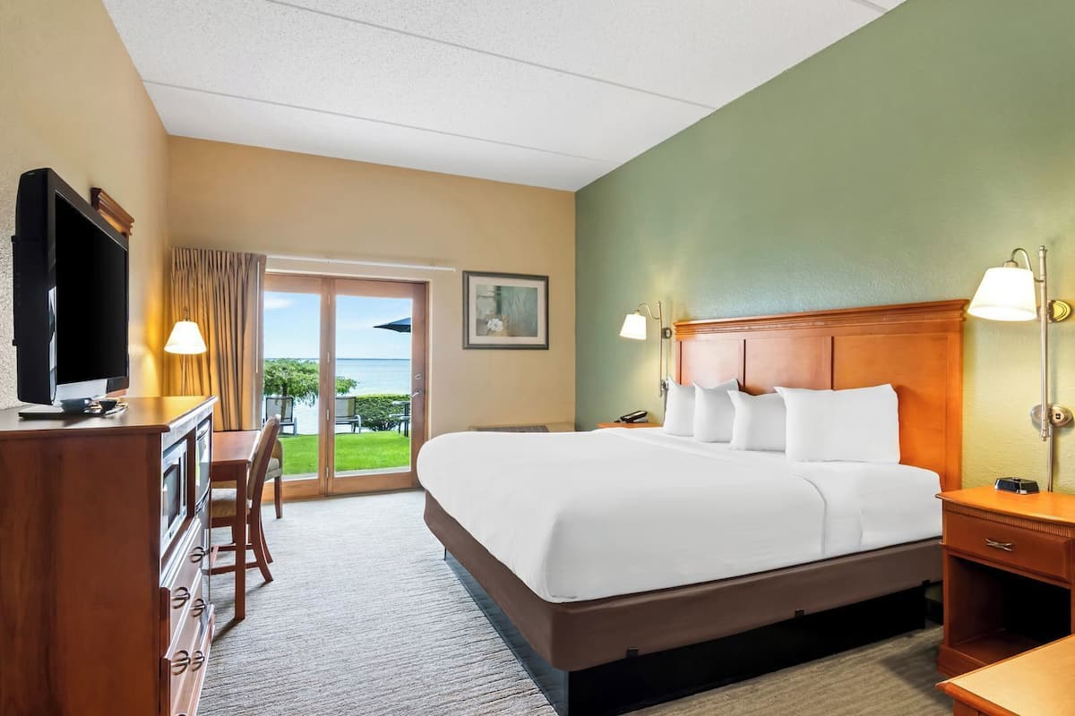 Quarto de hotel com uma cama grande, uma escrivaninha com televisão, uma cadeira e vista para o exterior.