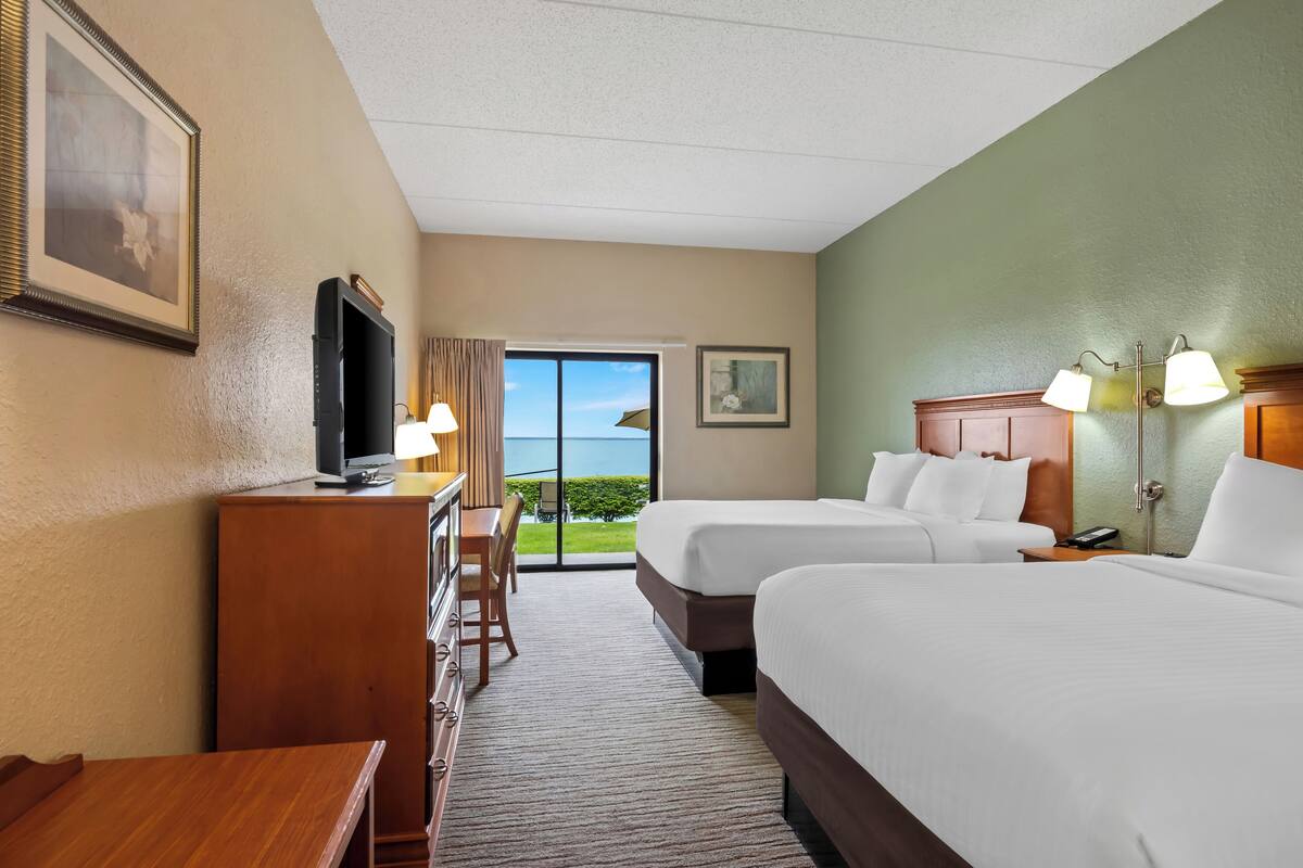 Quarto de hotel com duas camas, uma escrivaninha, televisão e vista para o mar.