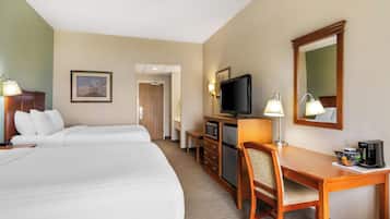 Quarto de hotel com duas camas, uma escrivaninha com cadeira, televisão, cafeteira e espelho.