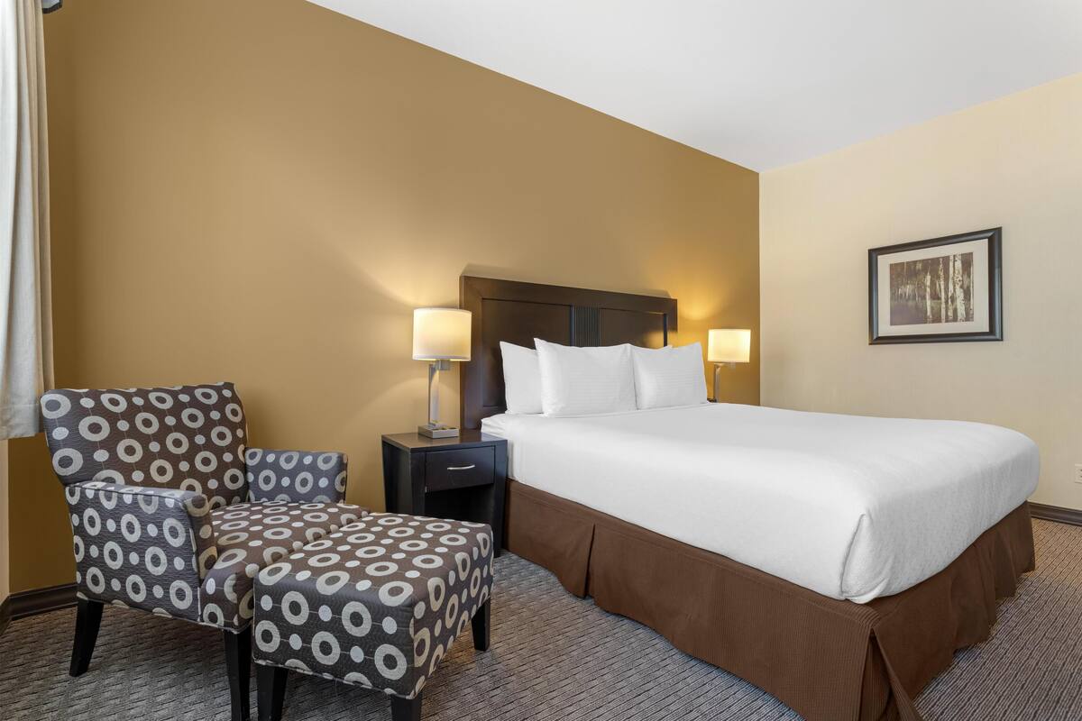 Quarto de hotel com uma cama grande, uma cadeira, uma mesa de cabeceira e uma luminária.