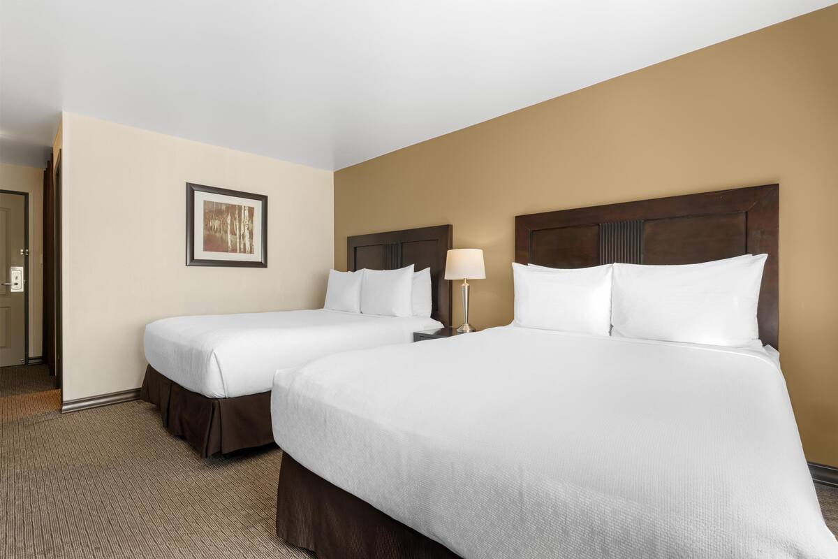 Quarto de hotel com duas camas, um quadro na parede e uma luminária na mesa de cabeceira.