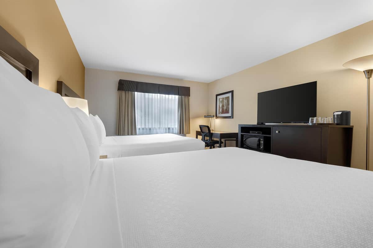 Quarto de hotel com duas camas, uma escrivaninha, uma televisão e uma luminária.
