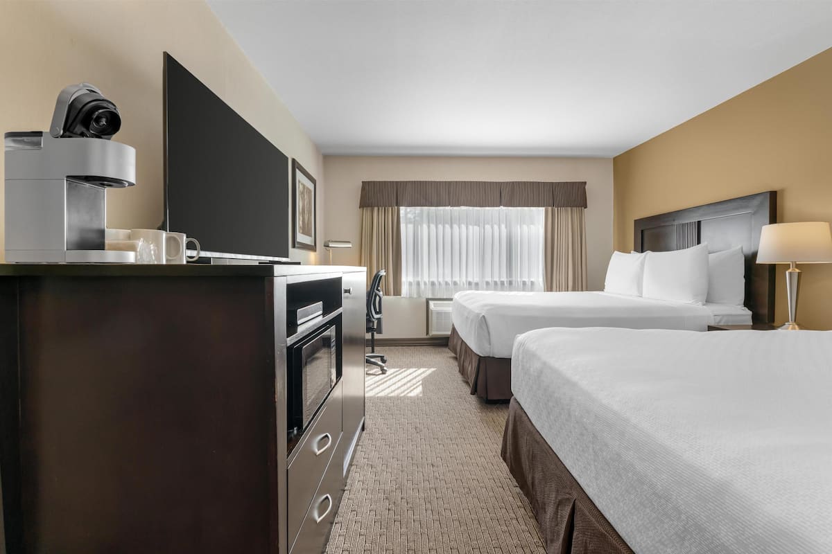 Quarto de hotel com cama, escrivaninha com cafeteira, televisão e janela com cortinas.