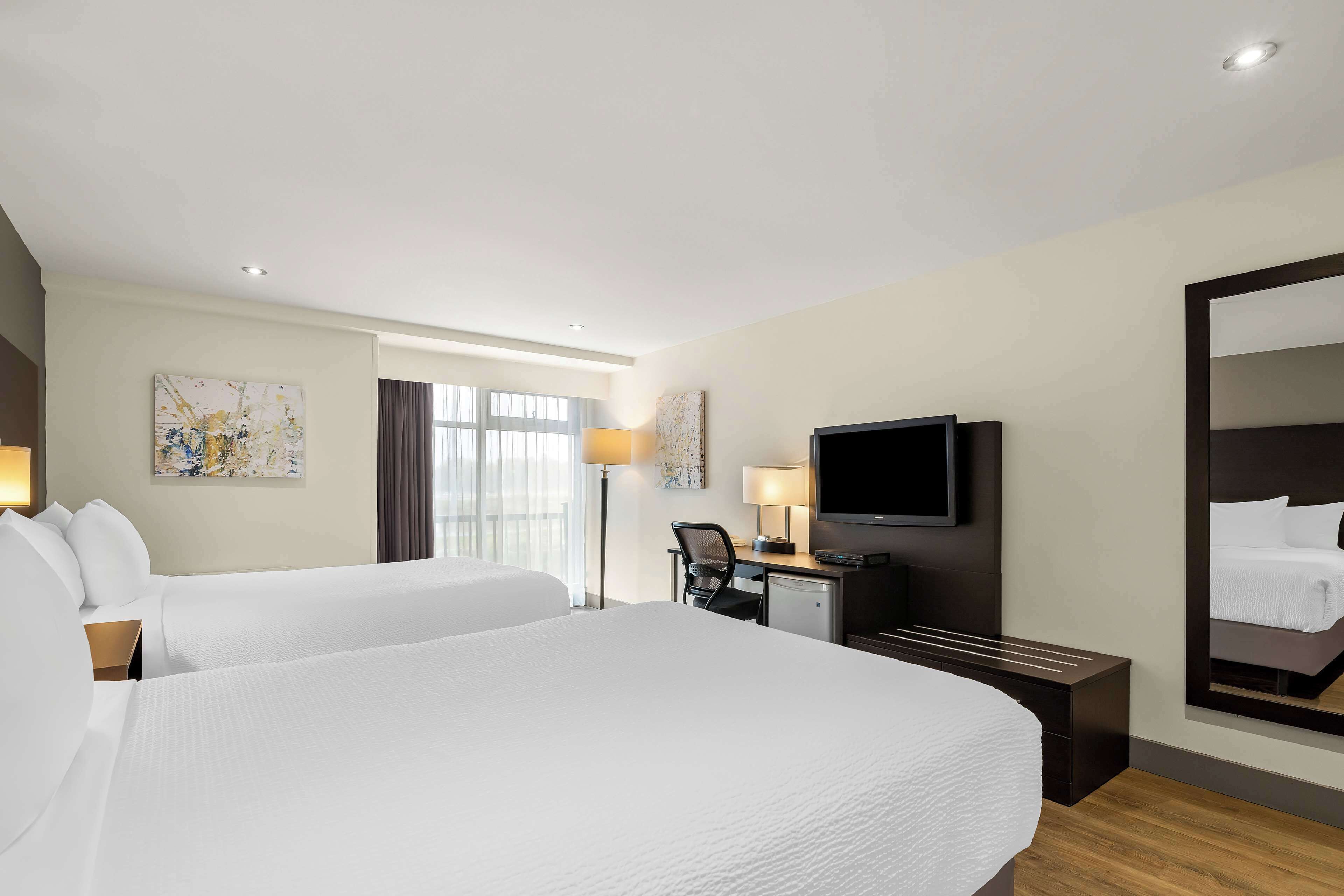 Quarto de hotel com duas camas, uma escrivaninha com televisão e obras de arte nas paredes.