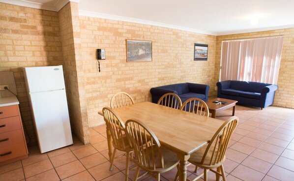 Um espaço compacto com cozinha, mesa de jantar para quatro pessoas, sofá azul e pequena mesa de centro.