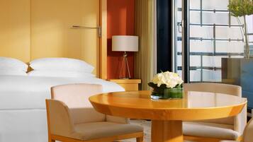 Quarto de hotel com cama, mesa redonda com cadeiras, abajur e um vaso com flores.