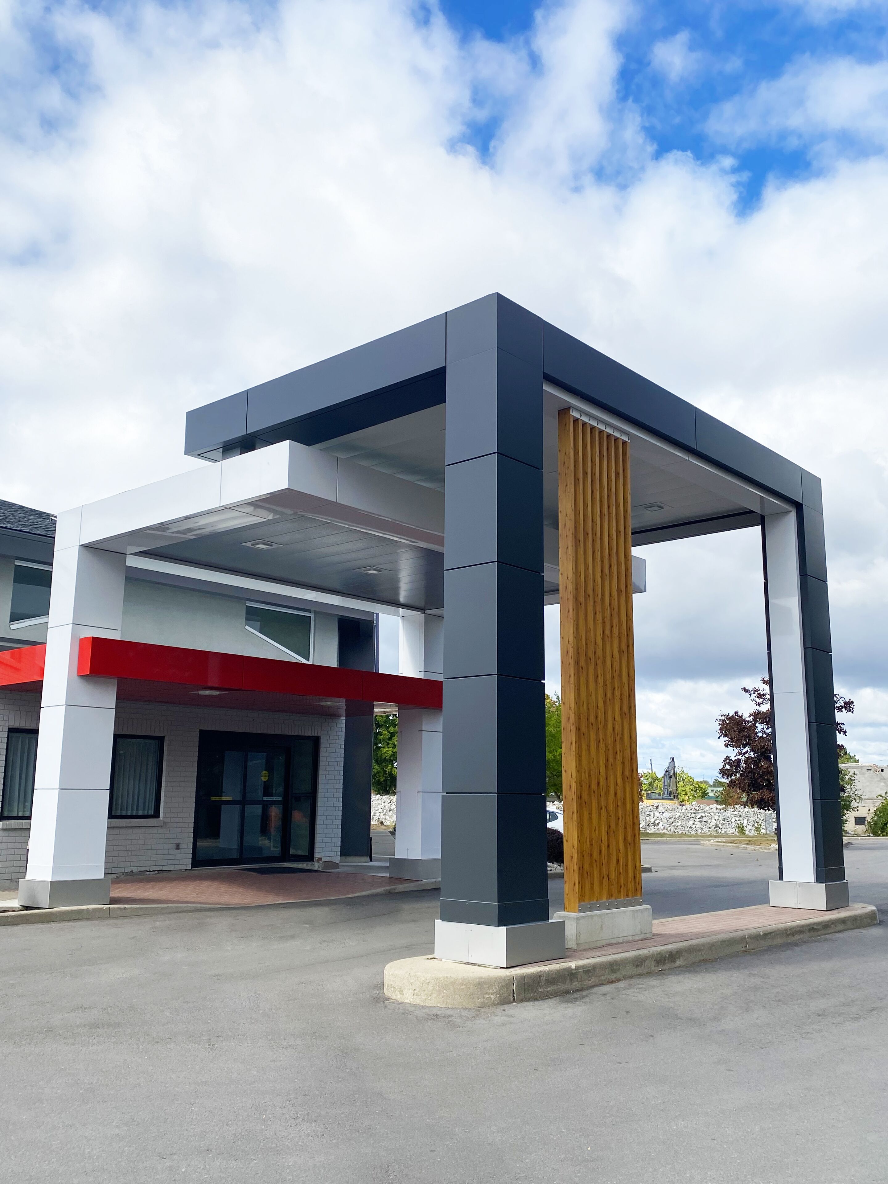 Um posto de combustível moderno com área de abastecimento coberta, fachada em vermelho e branco e uma grande coluna de madeira.