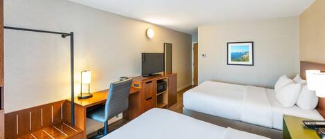 Quarto de hotel com duas camas, uma escrivaninha com cadeira, televisão e um quadro na parede.
