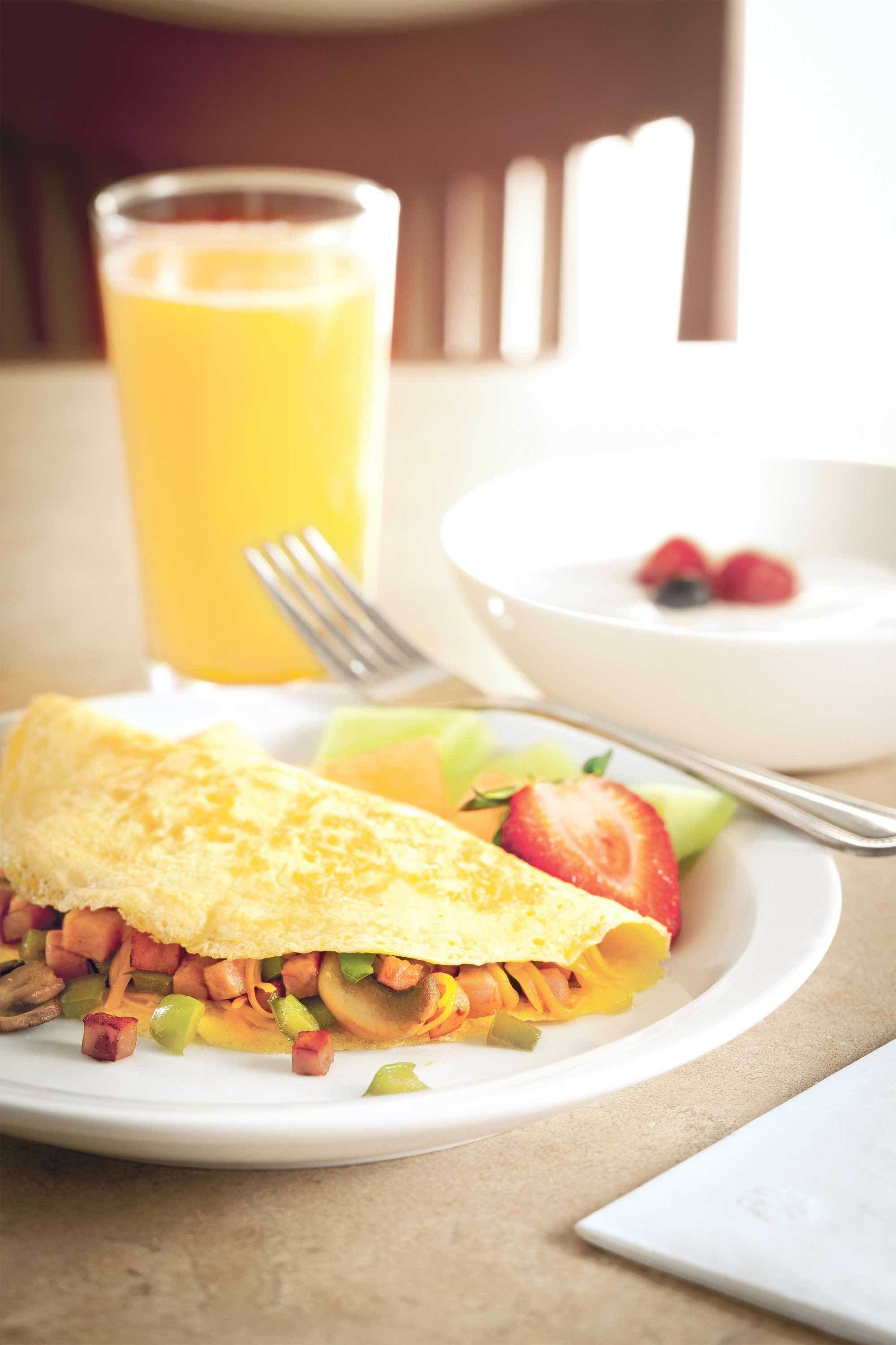 Prato de pequeno-almoço com omelete, legumes e um copo de sumo de laranja.