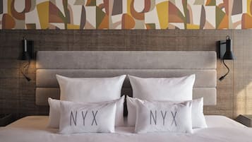 Cama arrumada com quatro almofadas, duas delas com as letras "NYX".