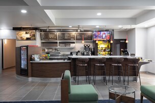Uma área de bar com balcão, banquetas e uma televisão exibindo uma partida esportiva.