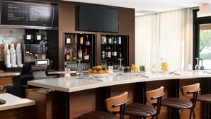 Uma área de bar com balcão extenso, banquetas, máquina de café e cardápio.