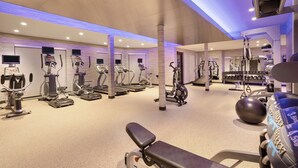Uma academia com esteiras, elípticos, aparelhos de musculação e um banco.