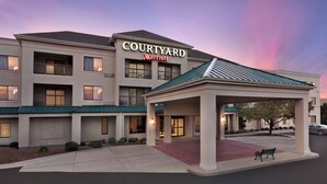 Um hotel Courtyard Marriott com entrada coberta, várias varandas e um caminho de tijolos vermelhos.
