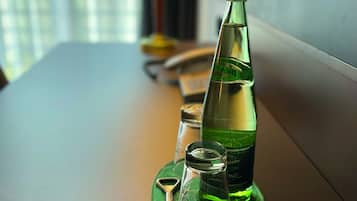 Uma garrafa de líquido verde sobre uma mesa com um apoio de copos verde, um copo e um abridor de garrafa de metal.