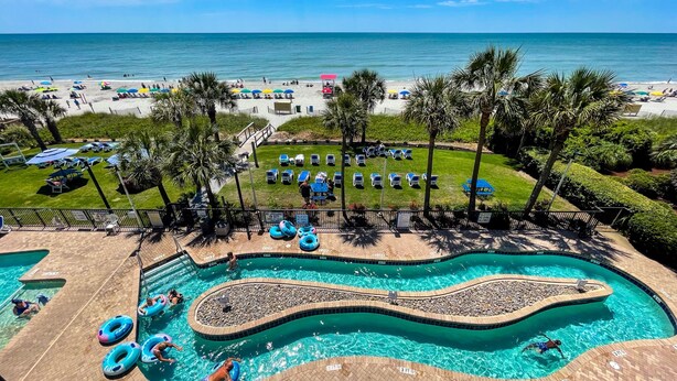 Uma área de piscina com design curvo, espreguiçadeiras e vista para a praia.