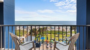 Varanda com vista para a praia, com cadeiras e guarda-sóis.