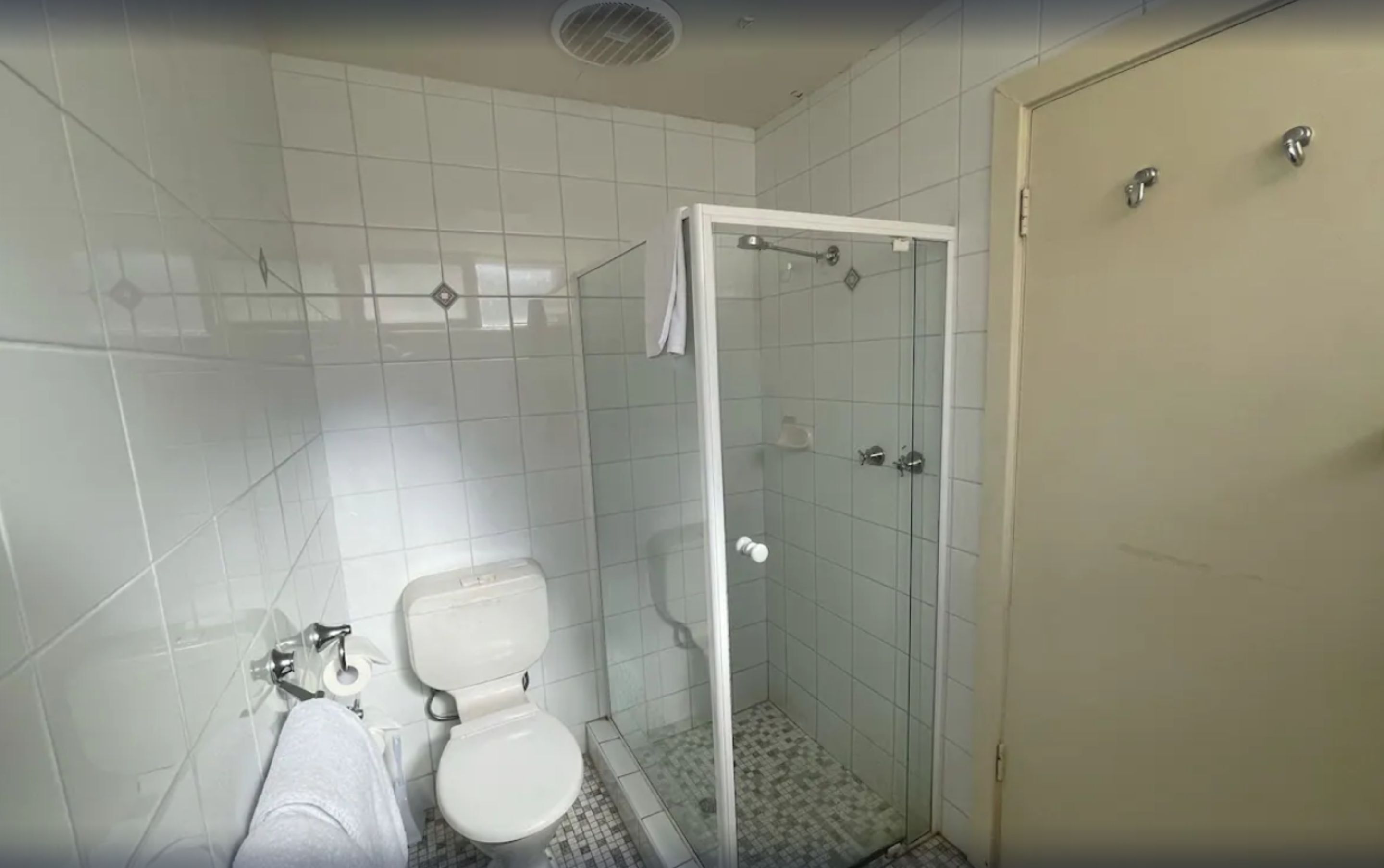 Casa de banho pequena com azulejos, vaso sanitário, cabine de duche e porta.