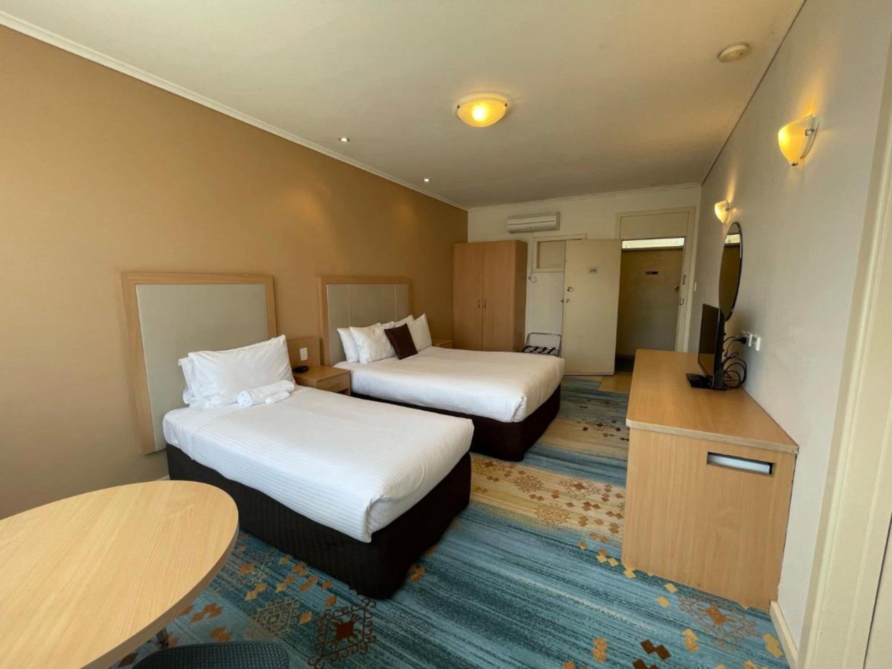 Quarto de hotel com duas camas, uma escrivaninha e um espelho.