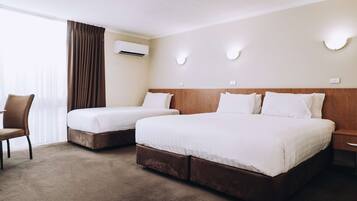 Quarto de hotel com duas camas, uma cadeira e uma mesa de cabeceira.