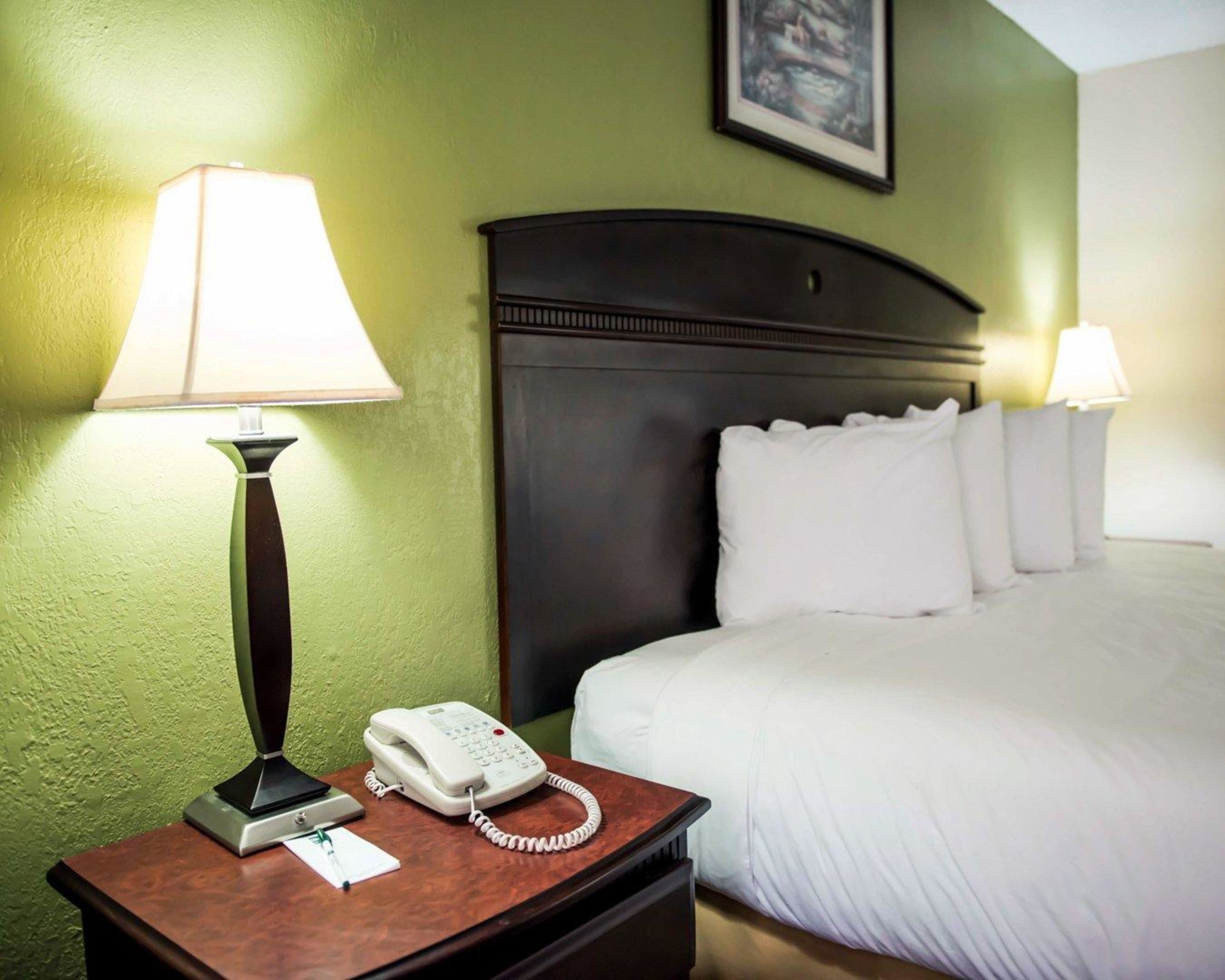Quarto de hotel com uma cama, duas luminárias de cabeceira, um telefone e um quadro na parede.