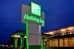 Placa do Holiday Inn com logotipo verde e branco, fachada de um edifício moderno e céu claro.