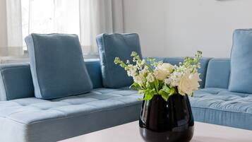 Uma sala de estar moderna com um sofá azul claro e um vaso preto com flores brancas sobre uma mesa branca.